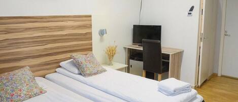 Quarto de hotel com duas camas, uma escrivaninha, uma televisão e uma porta.