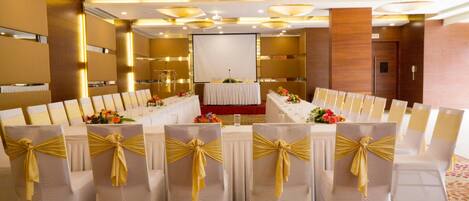 Uma sala de conferências com cadeiras brancas, palco e tela de projeção.