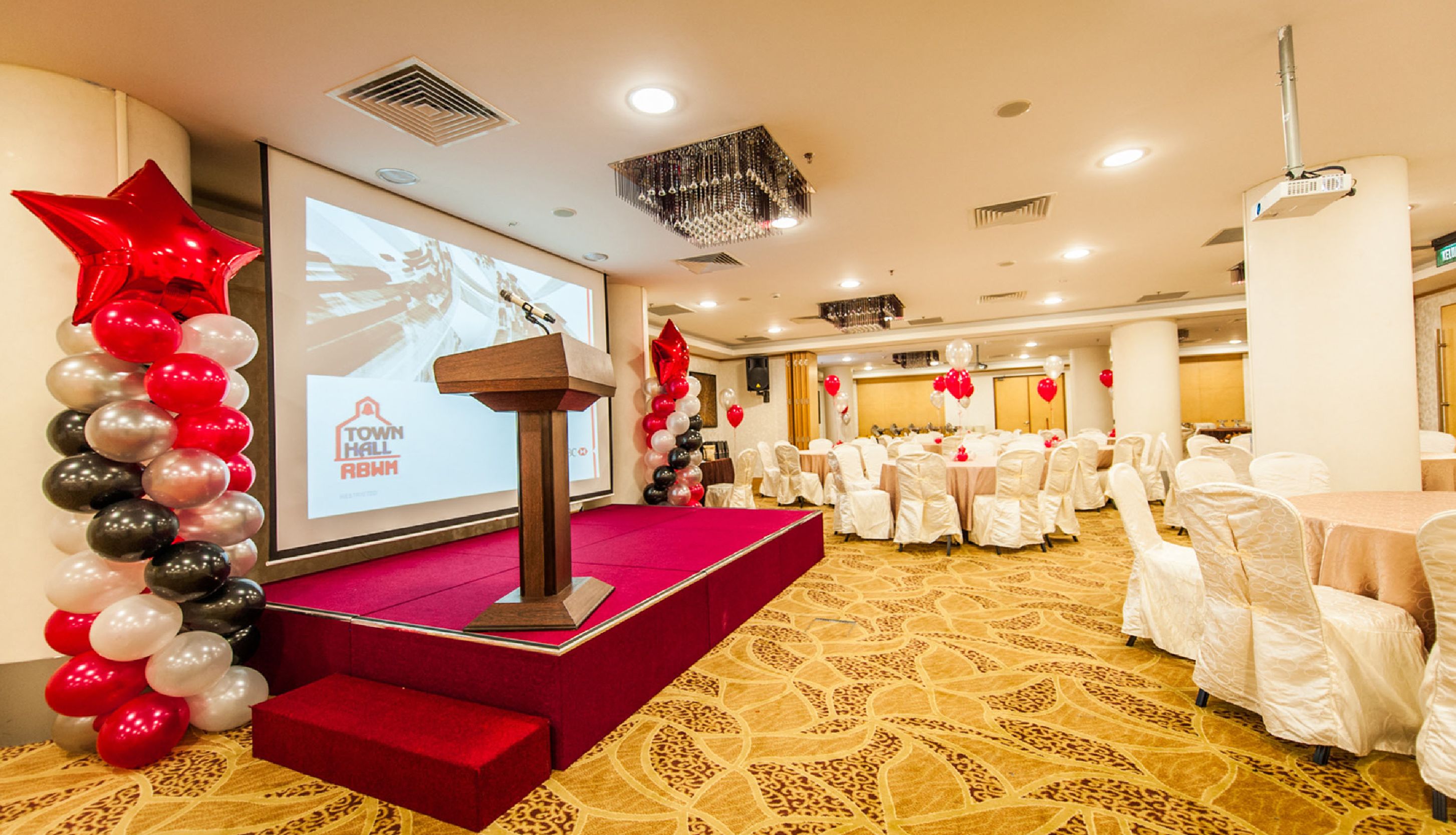 Uma sala de conferências com palco, um púlpito e uma tela exibindo uma apresentação.