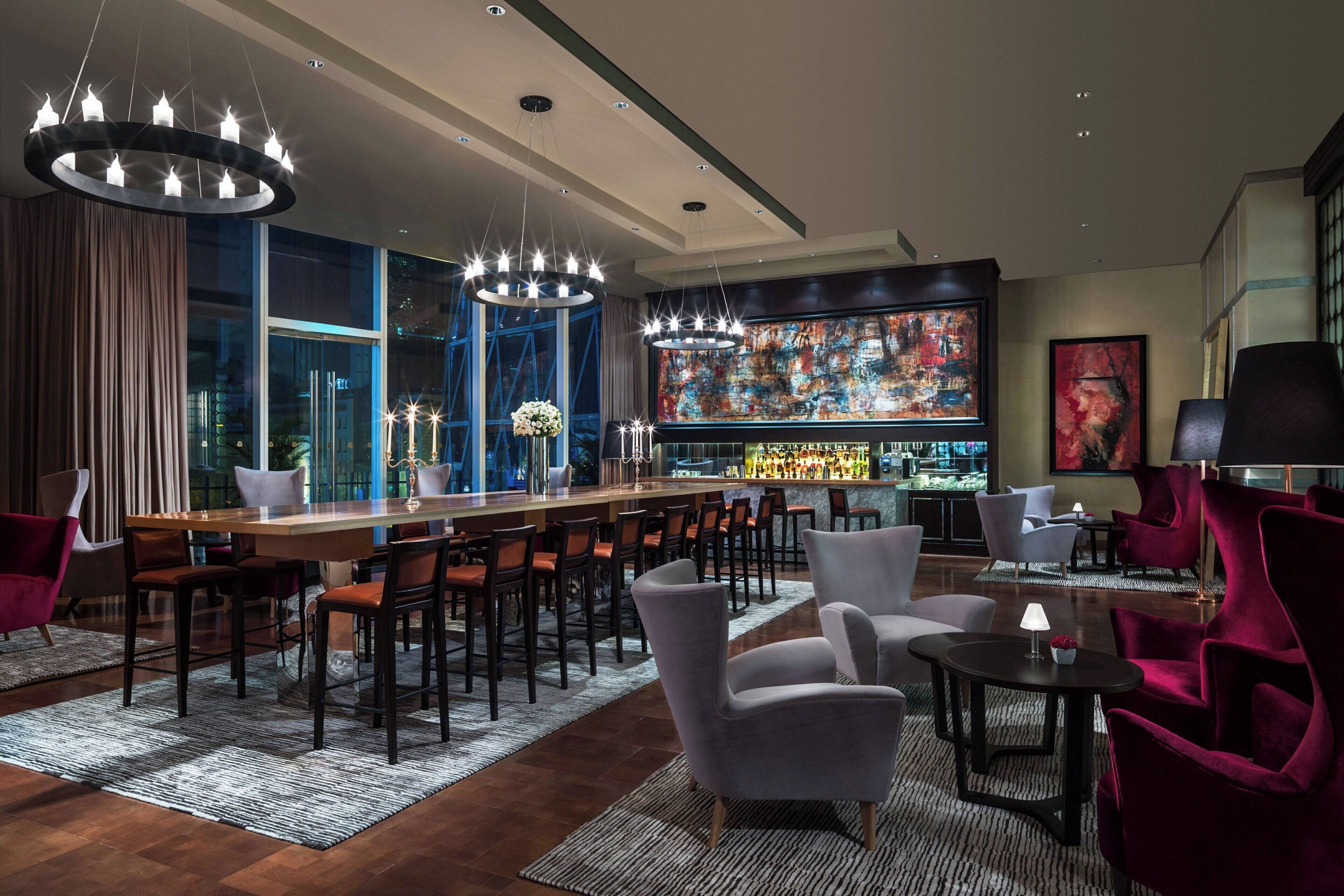 Uma área de bar moderna com um balcão comprido, vários banquetes e uma grande janela com vista para a cidade.