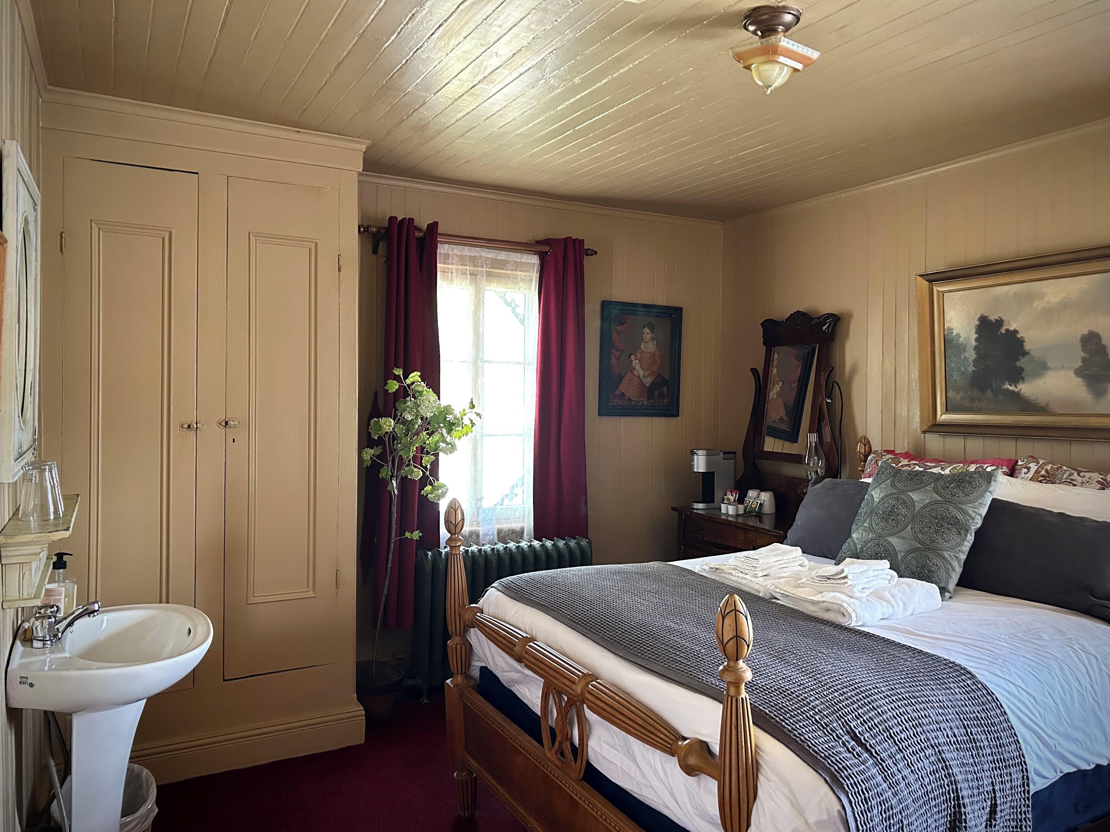 Quarto com cama, cômoda, toucador com pia e janela com cortinas.