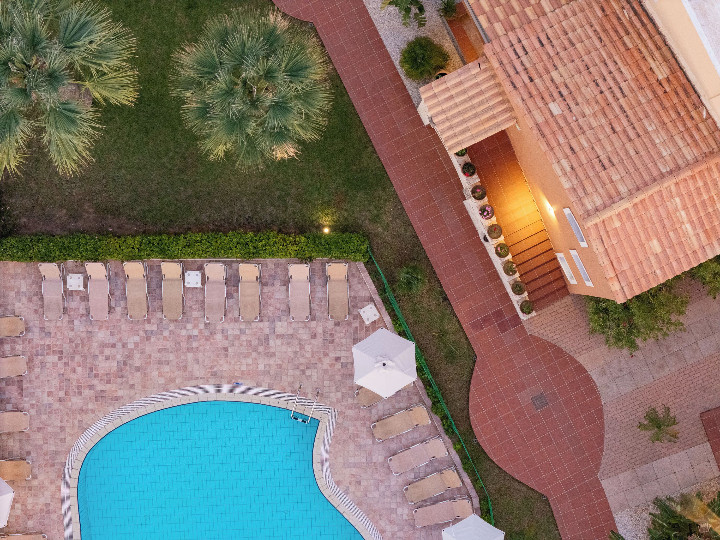 Vista aérea de uma área de piscina com espreguiçadeiras, um deck revestido de azulejos e palmeiras.