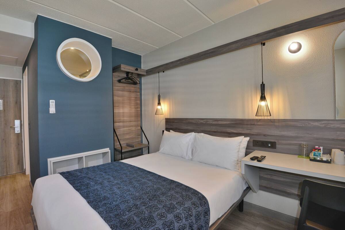 Quarto de hotel com uma cama, mesa de cabeceira e um espelho na parede.