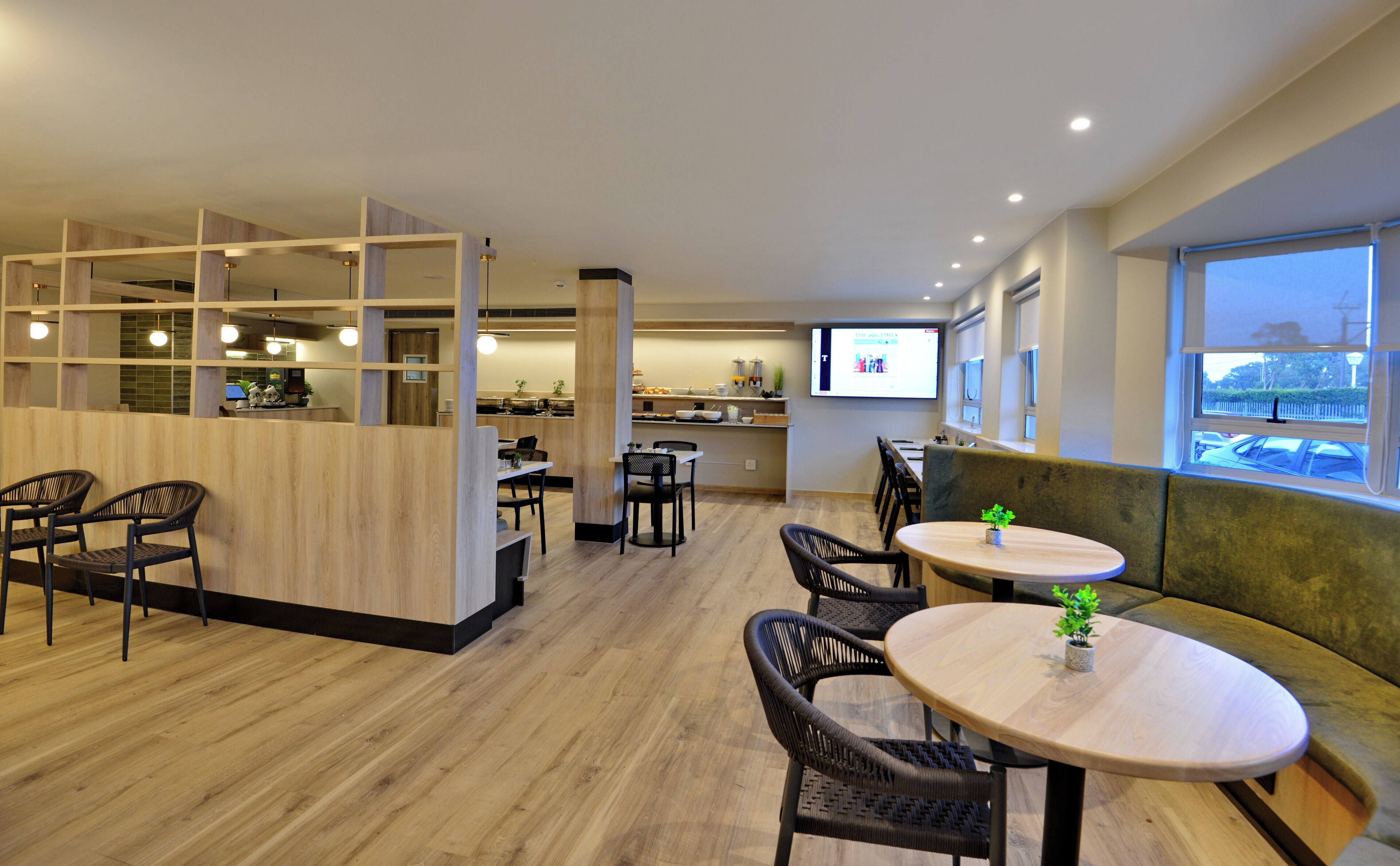 Uma sala de jantar moderna com piso de madeira, cadeiras de vime preto e uma mesa redonda com uma pequena planta.