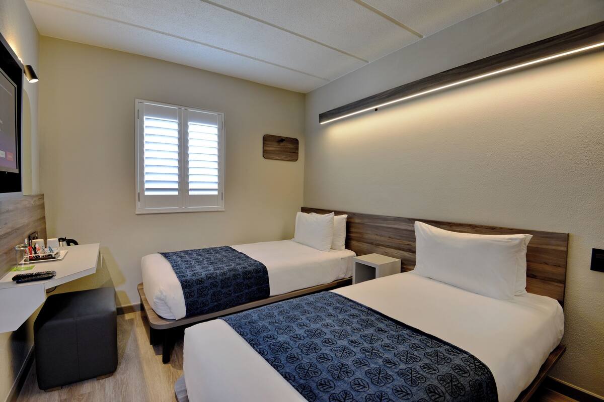Quarto de hotel com duas camas, uma mesa e uma janela.