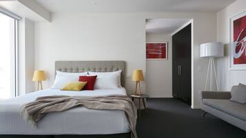 Quarto de hotel moderno com cama grande, duas luminárias de cabeceira, um sofá e um guarda-roupa.