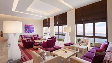 Uma sala de estar espaçosa com móveis roxos e beges, grandes janelas com vista para o mar e um design de teto moderno.