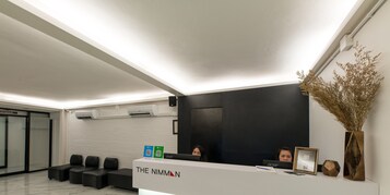 Uma área de recepção com balcão branco, parede preta e espaço para sentar.