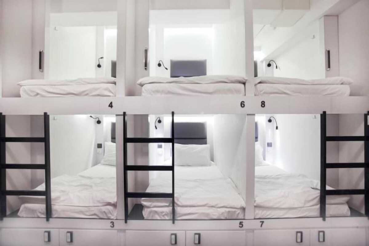 Quarto com beliches, escada em cada lateral, uma escrivaninha e uma janela.