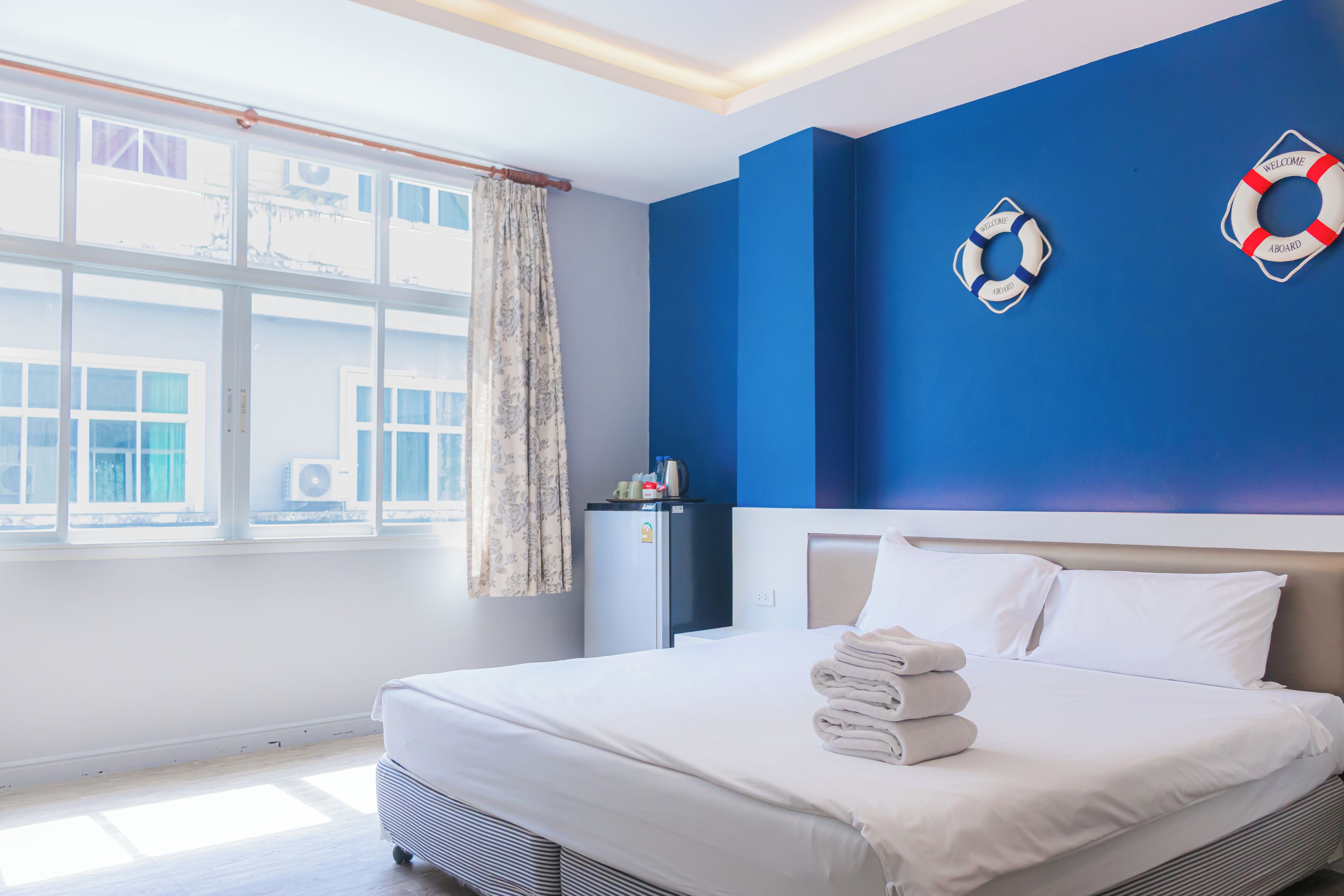 Quarto de hotel com uma cama, uma escrivaninha pequena e uma janela com cortinas.