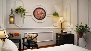 Quarto de hotel com cama, escrivaninha com luminária, cadeira, armário e plantas suspensas na parede.