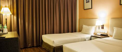 Quarto de hotel com duas camas, uma mesa de cabeceira com abajur, um quadro na parede e cortina.