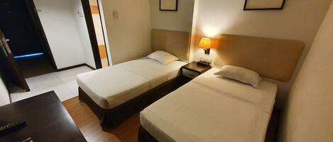 Quarto de hotel com duas camas de solteiro, uma mesa de cabeceira com abajur, um controle remoto e um quadro na parede.
