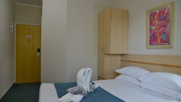 Quarto de hotel com uma cama, um guarda-roupa de madeira, um cobre-leito azul e um quadro colorido na parede.