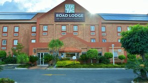 Um hotel com uma placa que diz "Road Lodge by City Lodge Hotels", fachada de tijolos, várias janelas e estacionamento.