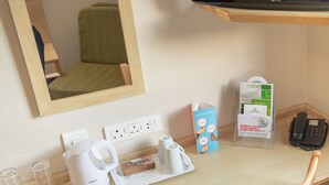 Quarto de hotel com escrivaninha de madeira, espelho, telefone, cafeteira, caixa de lenços e pequena mesa com chávenas e um copo.