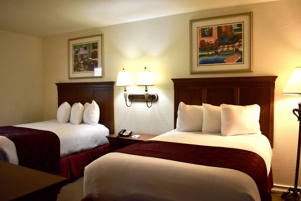 Quarto de hotel com duas camas, uma mesa de cabeceira, uma luminária e duas luminárias fixadas na parede.