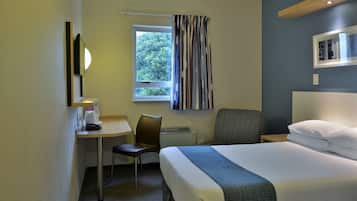 Quarto de hotel com cama, escrivaninha, cadeira e janela com cortinas.