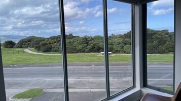Quarto com grandes janelas com vista para uma estrada e vegetação.