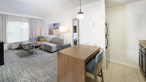 Quarto de hotel moderno com área de estar, mesa de jantar e cozinha compacta.