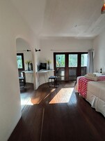 Quarto com cama, escrivaninha e televisão. Janela com vista para o verde.