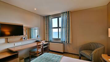 Quarto de hotel com cama, escrivaninha, cadeira, televisão e janela com cortinas.