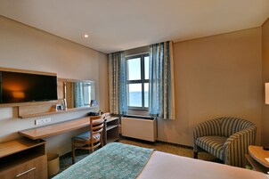 Quarto de hotel com cama, escrivaninha, cadeira, televisão e janela com cortinas.
