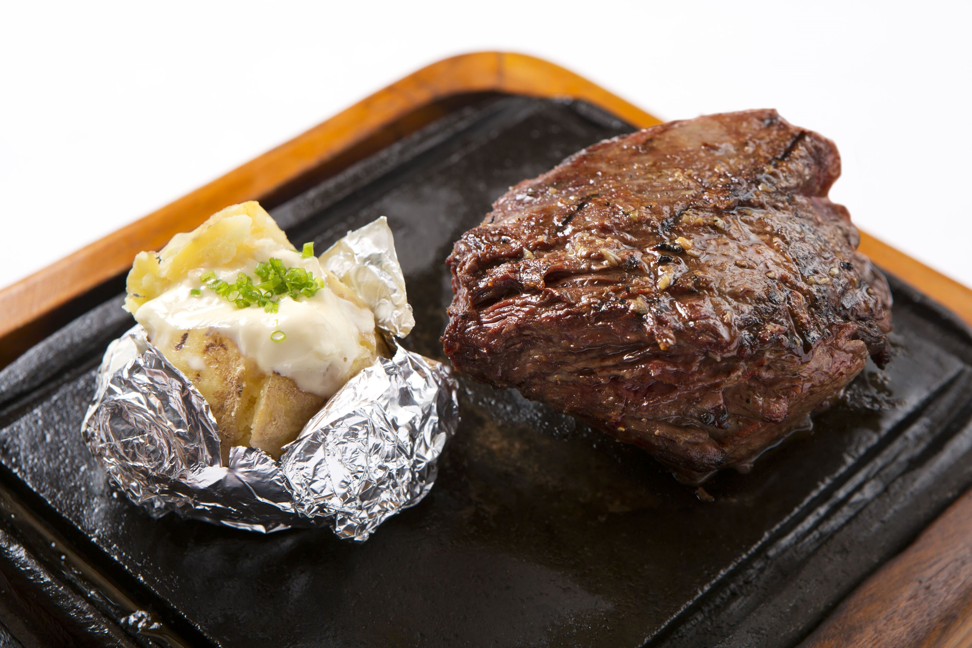Bife com batatas embrulhadas em papel alumínio sobre um prato de ardósia preta.