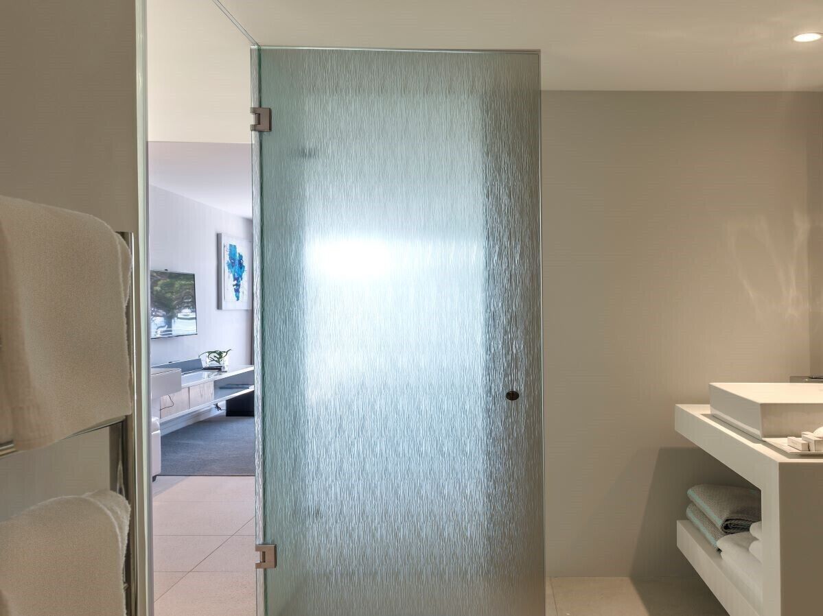 Casa de banho moderna com porta de vidro fosco, pia branca e suporte para toalhas.
