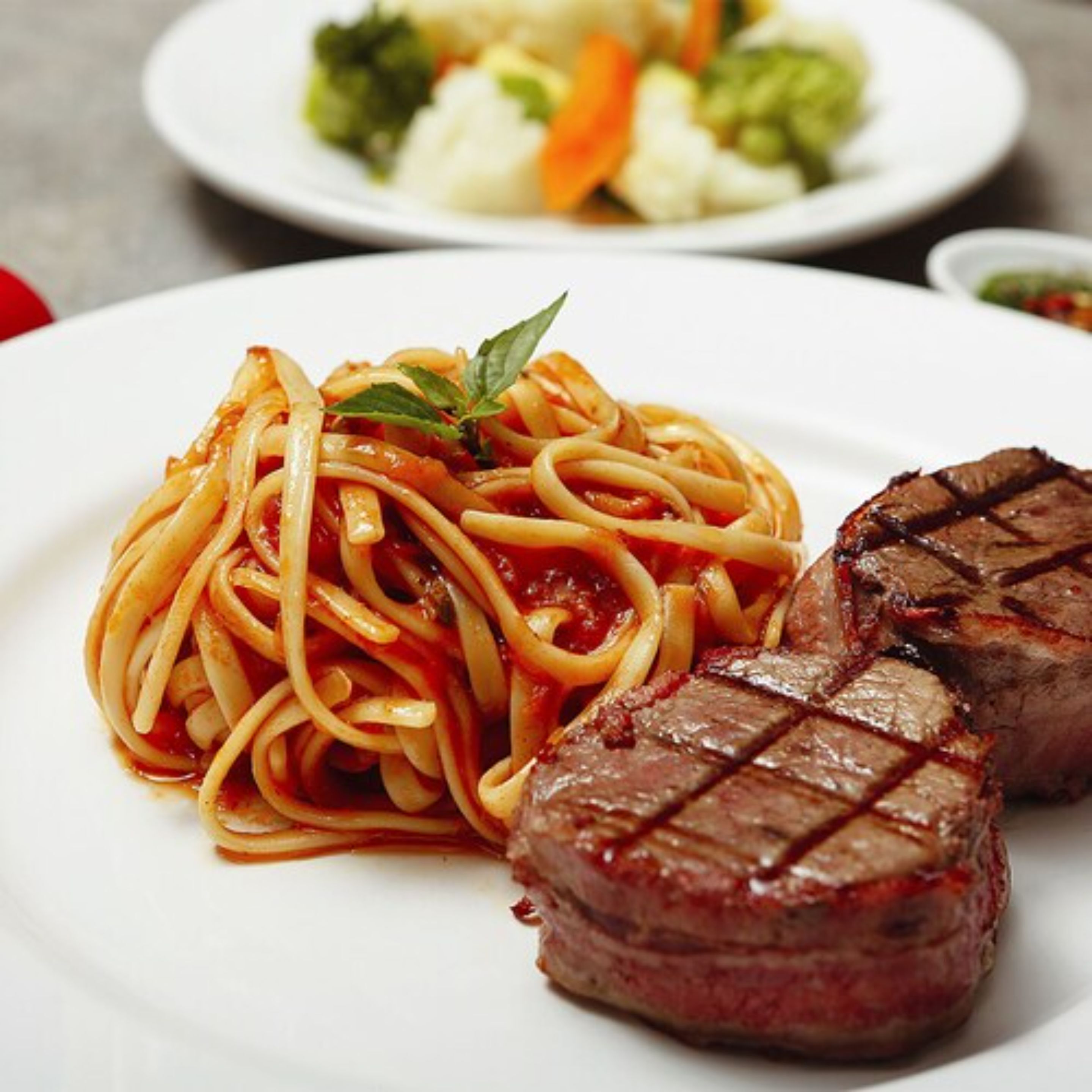 Um prato de espaguete com um bife grelhado no acompanhamento.