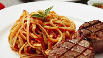 Um prato de espaguete com um bife grelhado no acompanhamento.