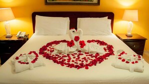 Quarto de hotel com cama bem arrumada, telefone na mesa de cabeceira e luminária na mesinha lateral.