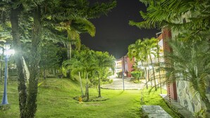 Vista noturna de um jardim bem iluminado, com um caminho que leva a um edifício.