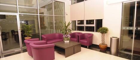 Um lobby moderno com área de estar, mesa de centro e plantas em vasos.