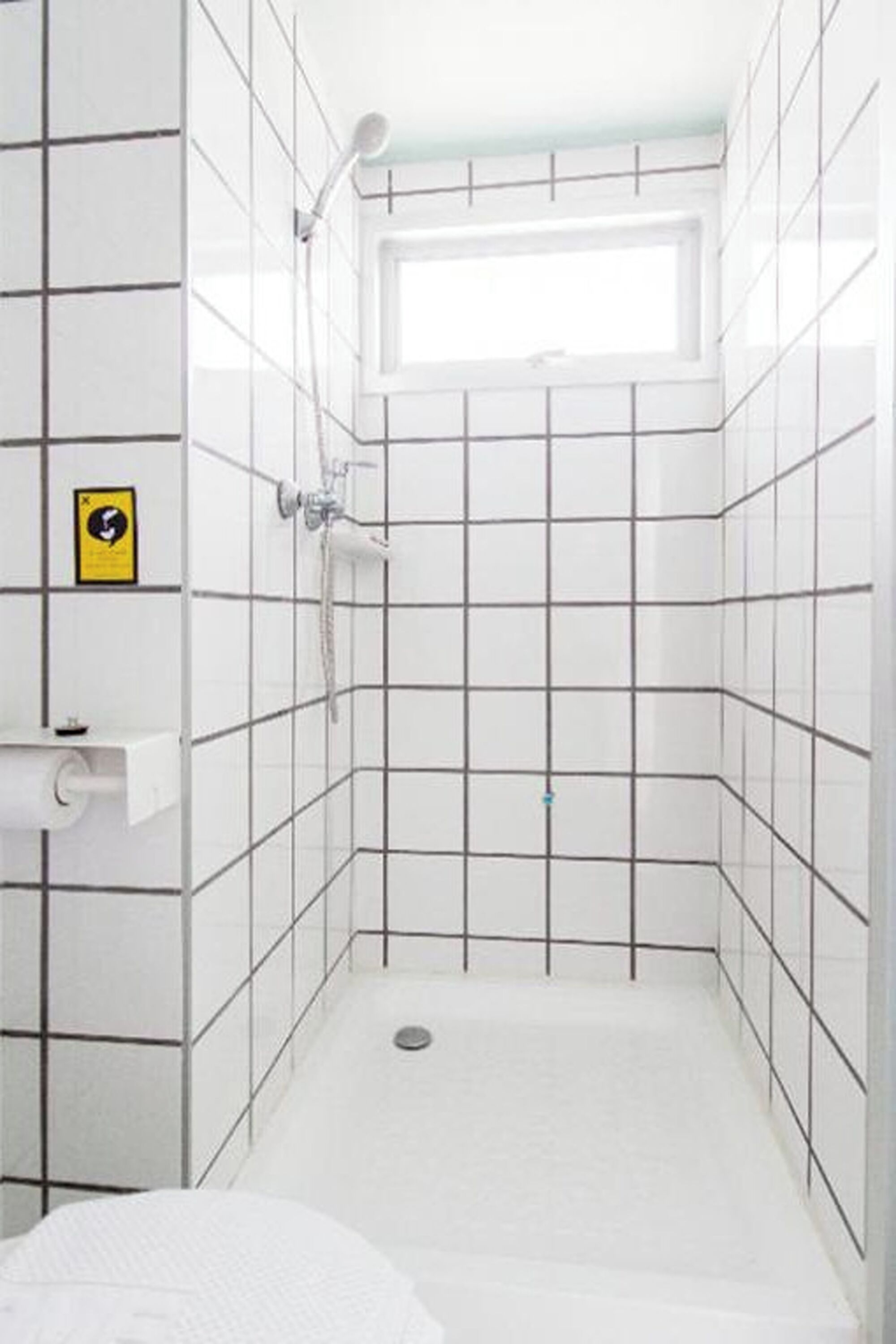 Um pequeno banheiro com azulejos, janela e porta-papel higiênico.