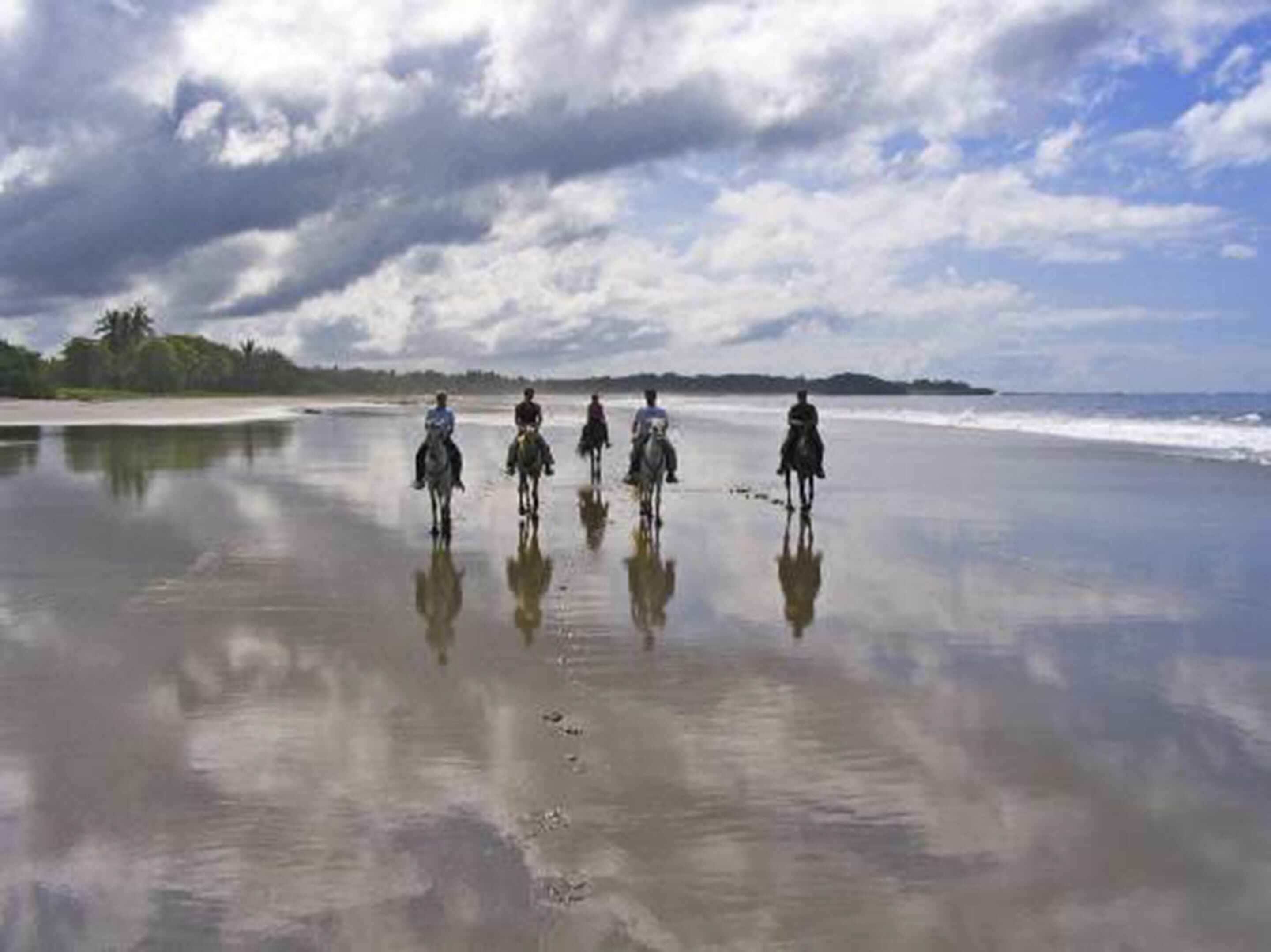 Uma praia com um grupo de pessoas a cavalo.
