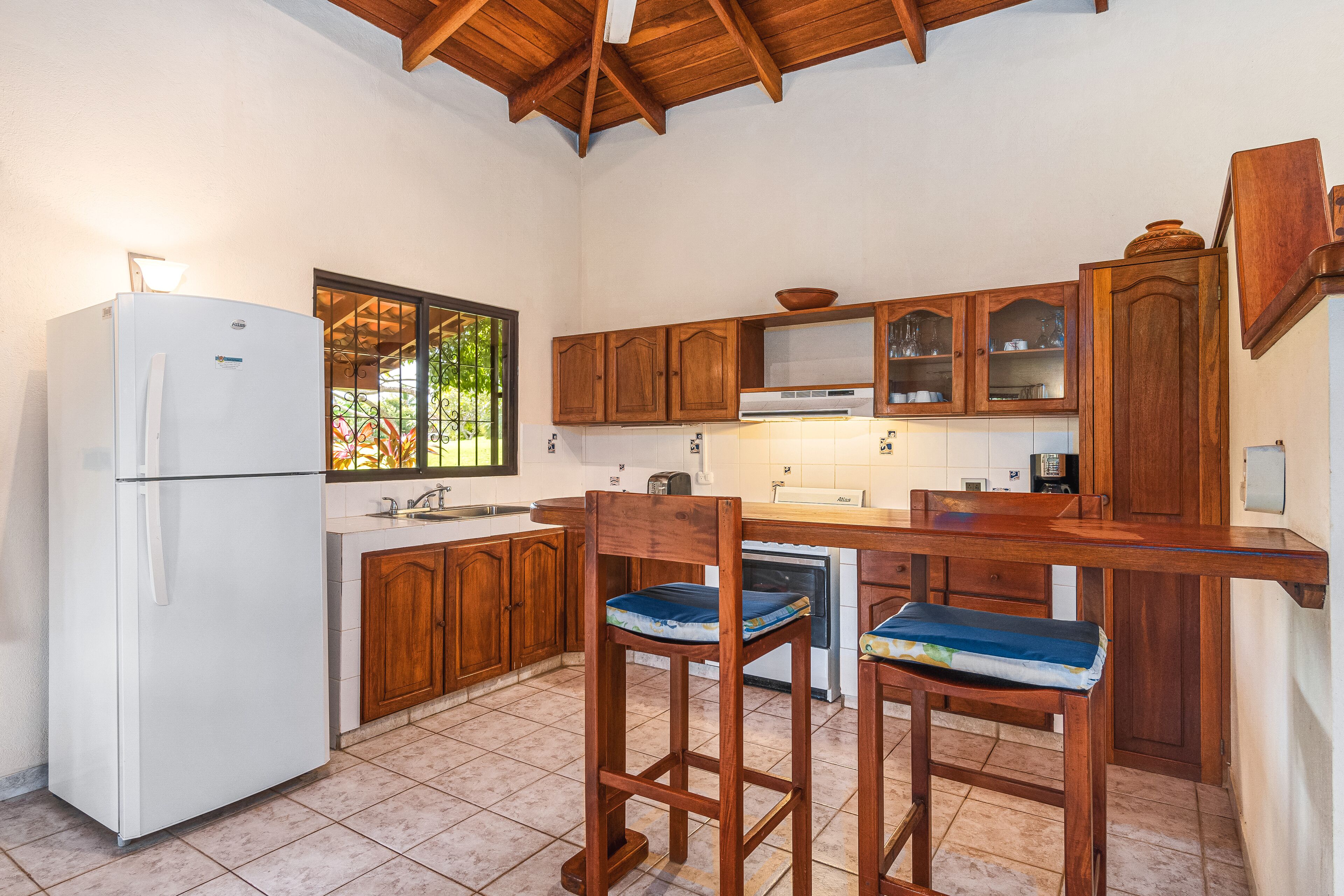 Uma cozinha compacta com armários de madeira, uma geladeira branca e dois banquetas.