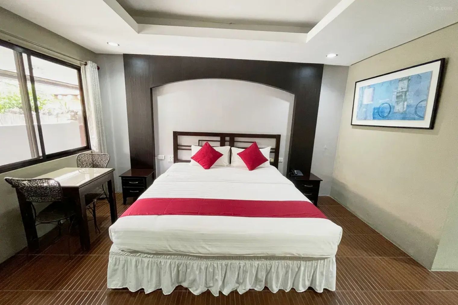 Quarto de hotel com cama, mesas de cabeceira, escrivaninha e uma janela.