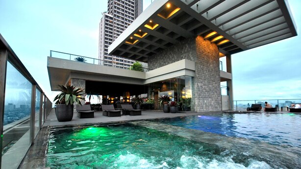 Piscina infinita no terraço com cachoeira, rodeada por espreguiçadeiras e plantas em vasos.