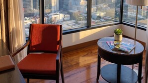 Quarto moderno com grandes janelas, uma cadeira vermelha, uma pequena mesa com uma planta e um abajur.