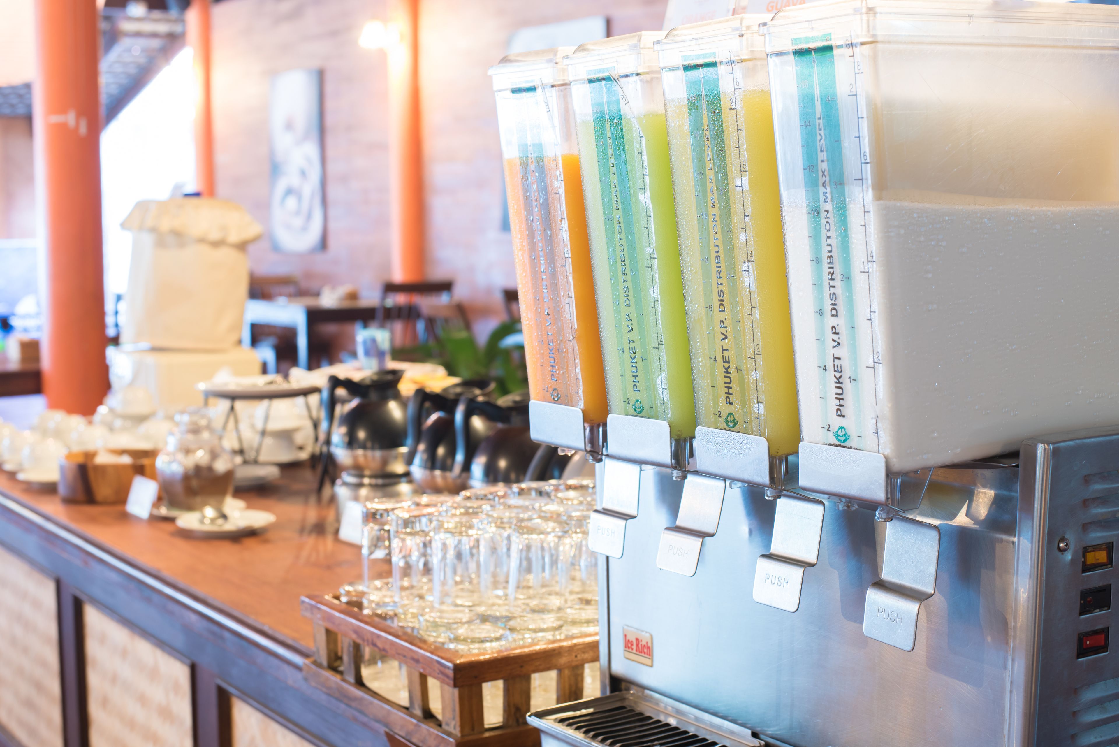 Dispensador de bebidas com várias opções, copos alinhados para servir e área de bar com diversos itens.