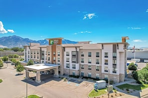 Edifício Holiday Inn Express com estacionamento, área coberta e montanhas ao fundo.