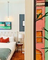 Quarto de hotel com cama, mesa de cabeceira com abajur, quadro na parede e janela com cortinas.