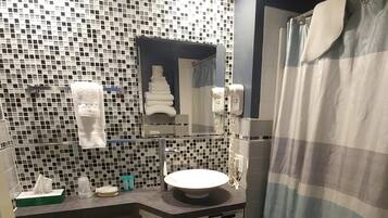Um banheiro com piso ladrilhado, vaso sanitário branco, pia com espelho acima e cortina de chuveiro.