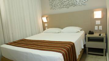 Quarto de hotel com cama, mesa de cabeceira com telefone e luminárias fixadas na parede.