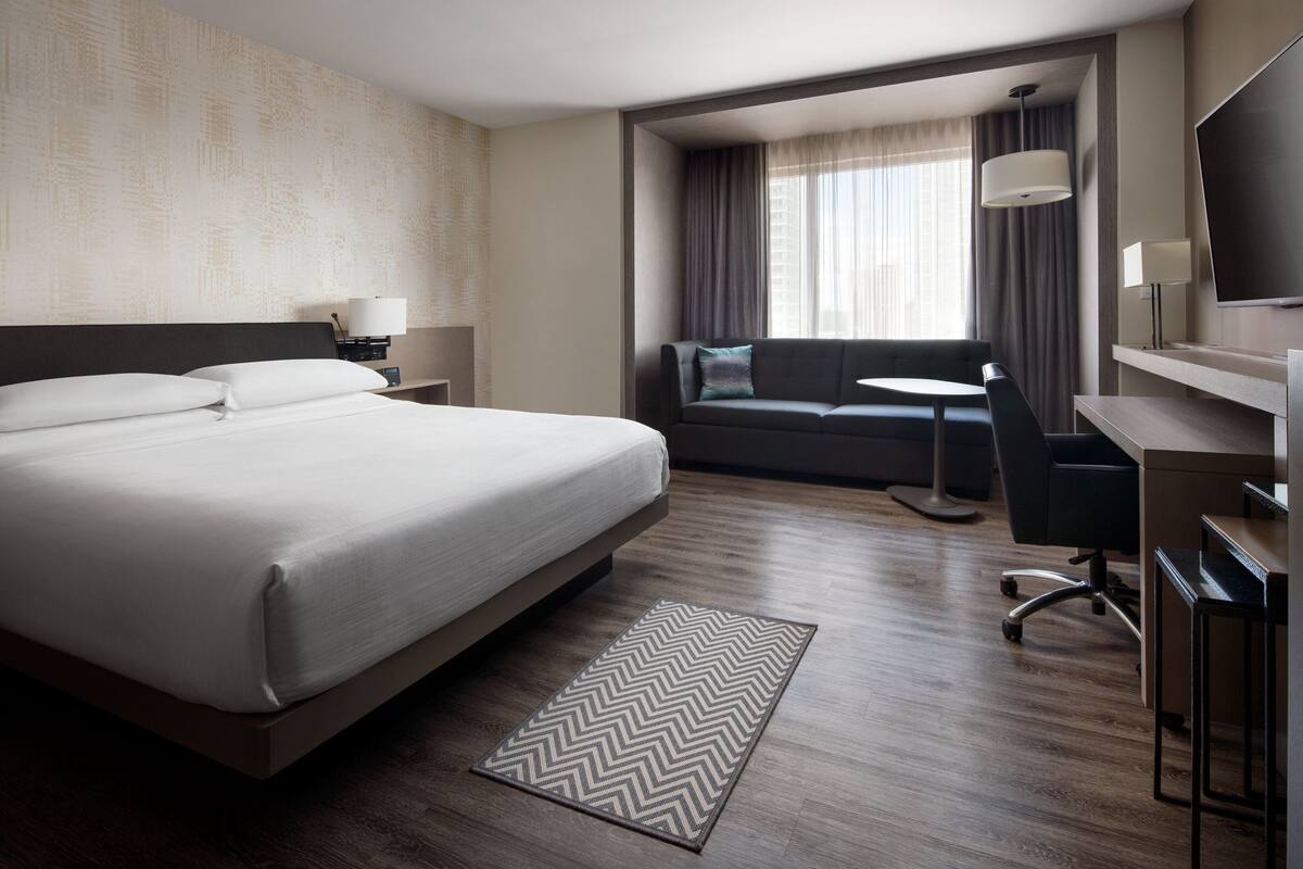 Quarto de hotel com uma cama grande, uma escrivaninha, um sofá e uma televisão.