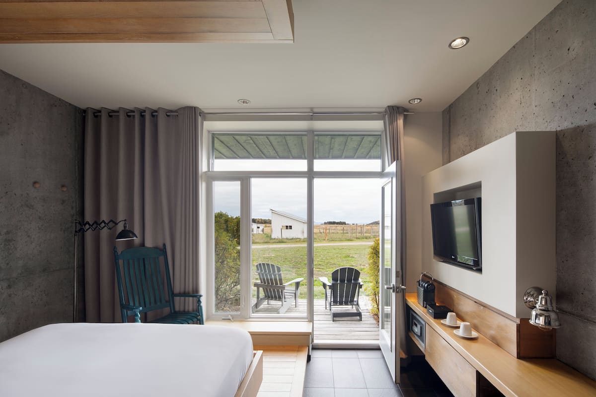 Quarto de hotel moderno com cama, televisão, secretária com máquina de café e vista para o exterior.