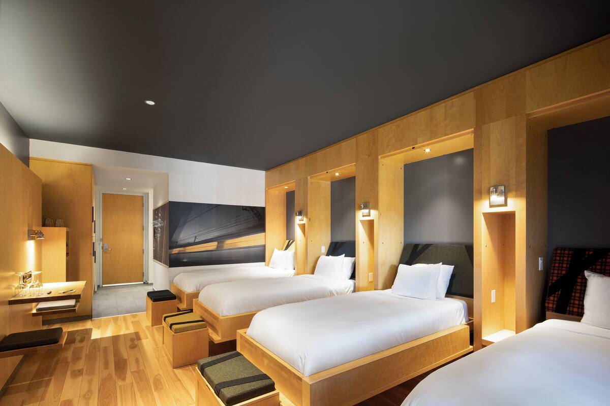Quarto de hotel moderno com três camas, painéis de madeira e uma grande pintura abstrata na parede.