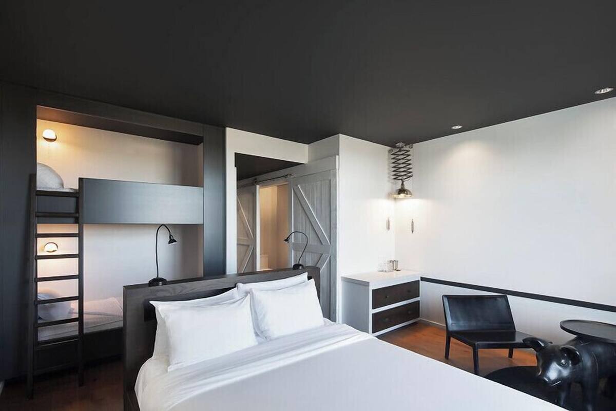Quarto de hotel moderno com cama, mesa de cabeceira, poltrona e escrivaninha com cadeira.