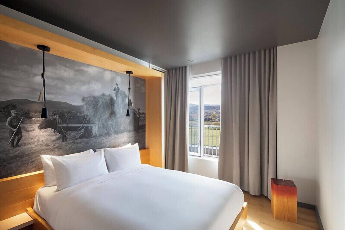 Quarto de hotel com uma cama grande, um quadro na parede, vista para a cidade e uma mesa de cabeceira de madeira.